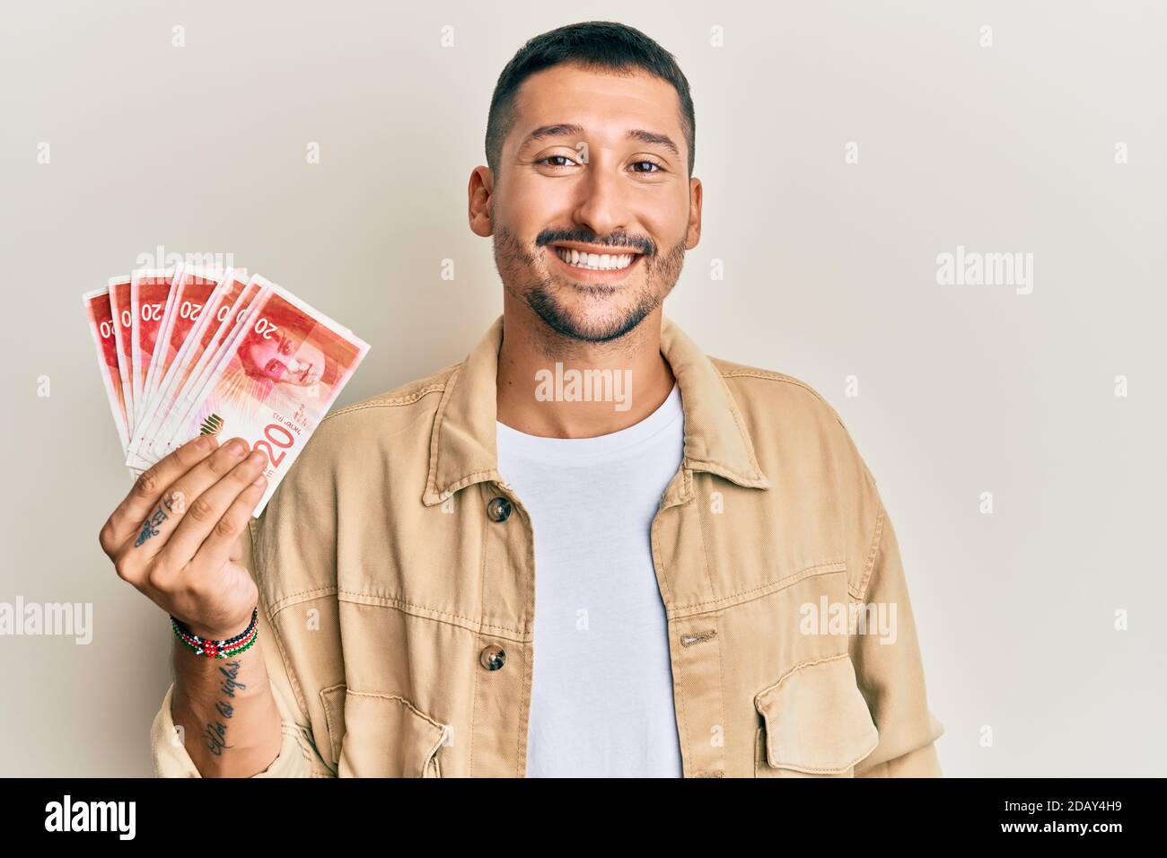 Handsome man with tattoos holding 20 israel shekels banknotes looking ...