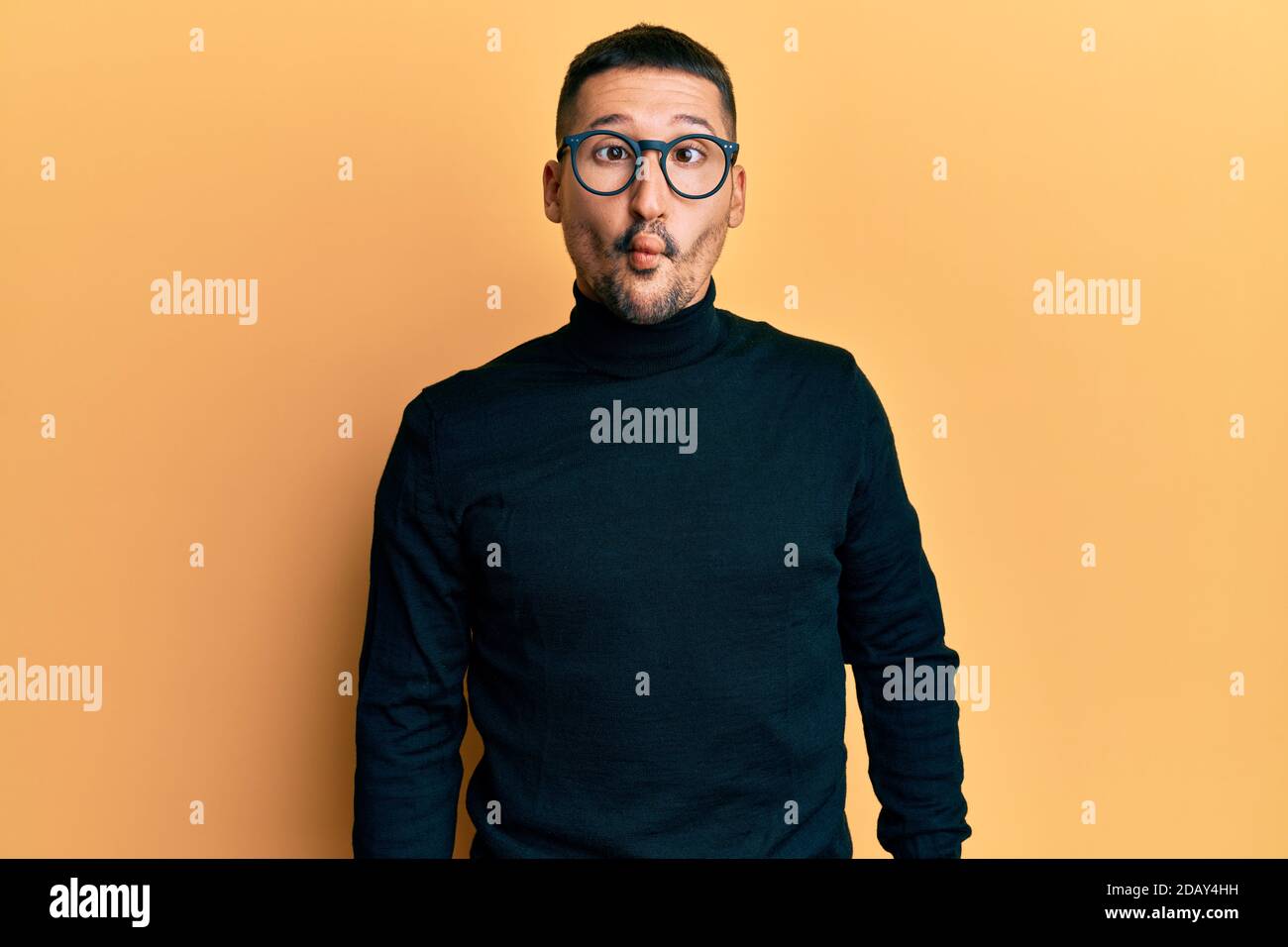 Handsome man with tattoos wearing turtleneck sweater and glasses making ...