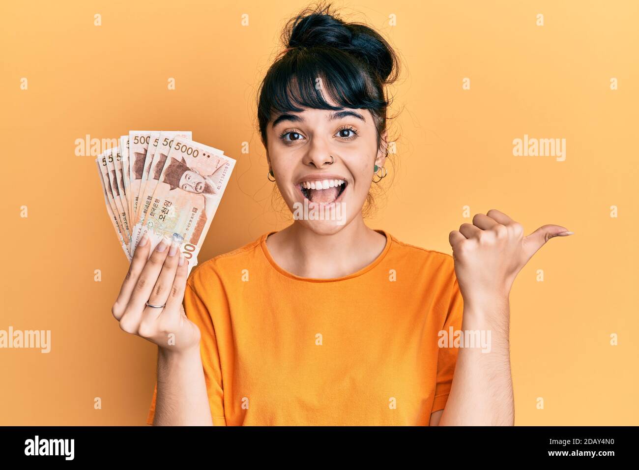 Young hispanic girl holding 5000 south korean won banknotes pointing ...