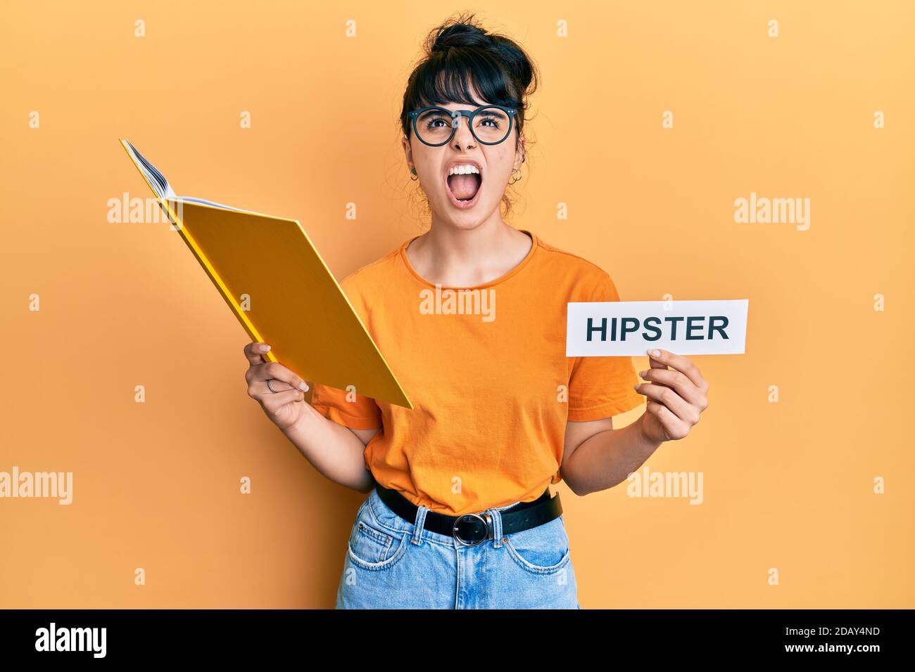 Young hispanic girl reading book and holding paper with hipster message ...