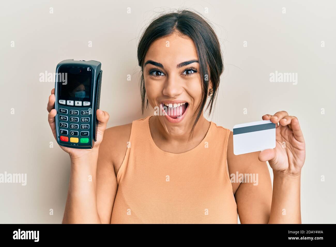 Young brunette woman holding dataphone and credit card celebrating ...