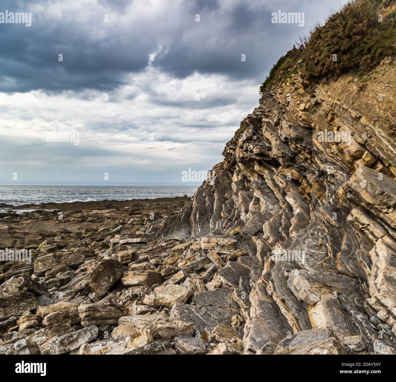 Rocky beach surrounded by cliffs and sea under a cloudy sky on a gloomy ...