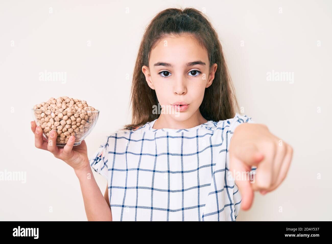 Cute hispanic child girl holding chickpeas bowl pointing with finger to ...