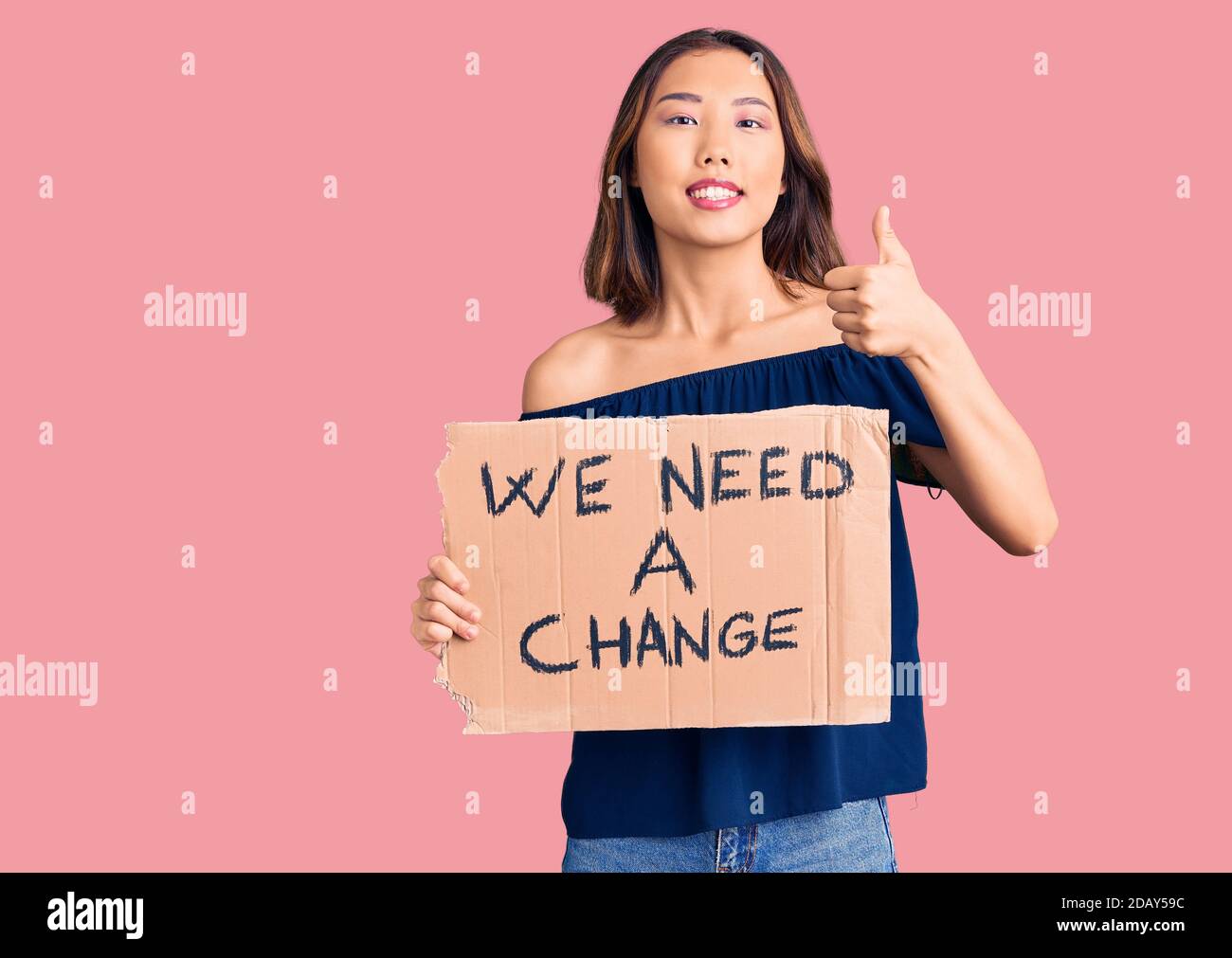 Young beautiful chinese girl holding we need a change banner smiling ...