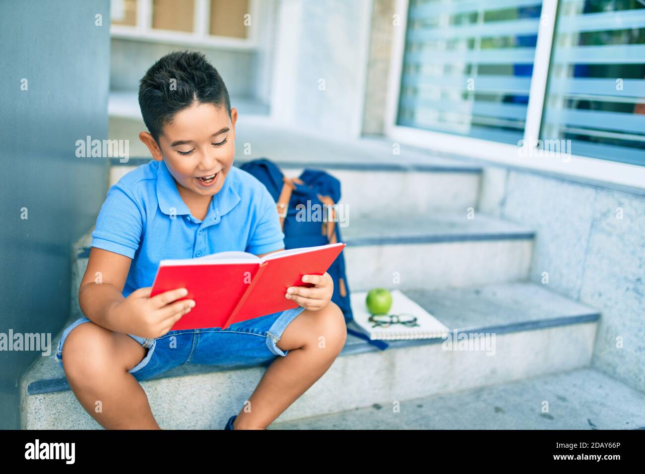 Adorable student boy reading book sitting on the stairs at school Stock ...