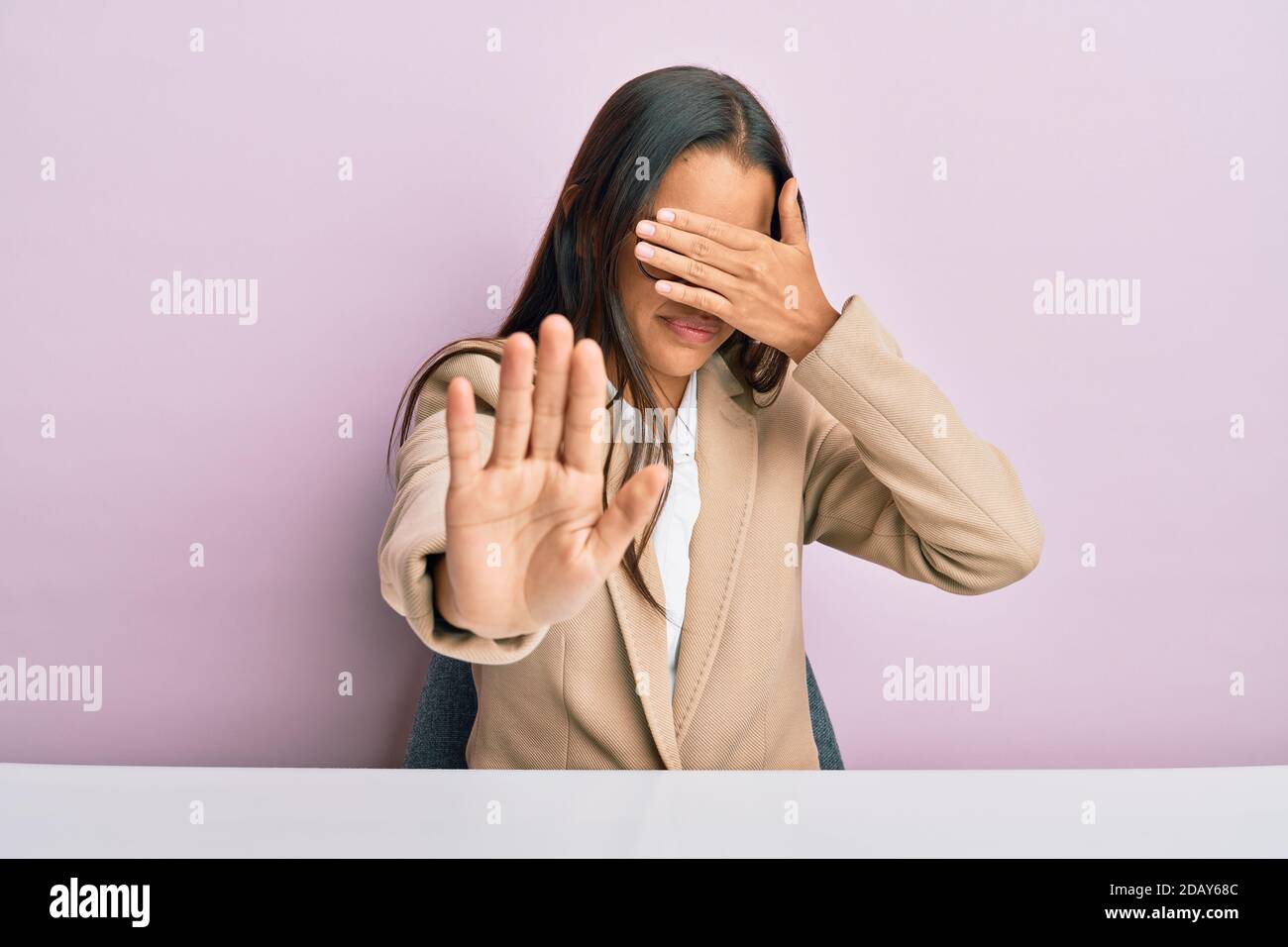 Beautiful hispanic woman working at the office covering eyes with hands ...