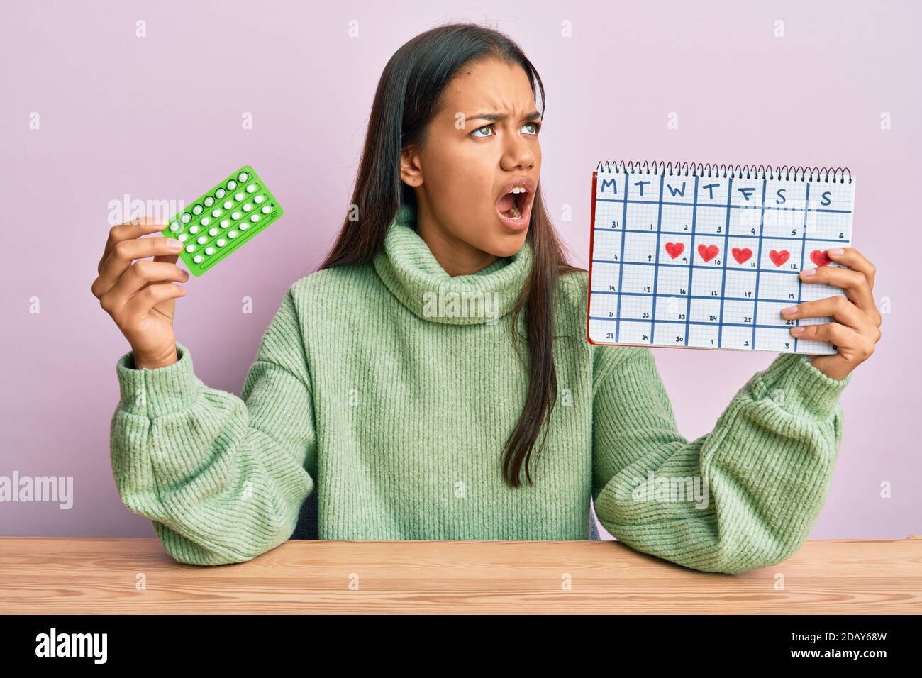 Beautiful hispanic woman holding birth control pills angry and mad ...