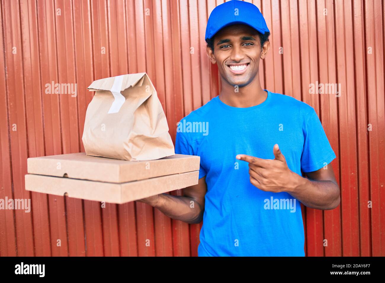 African delivery man wearing courier uniform outdoors holding take away ...