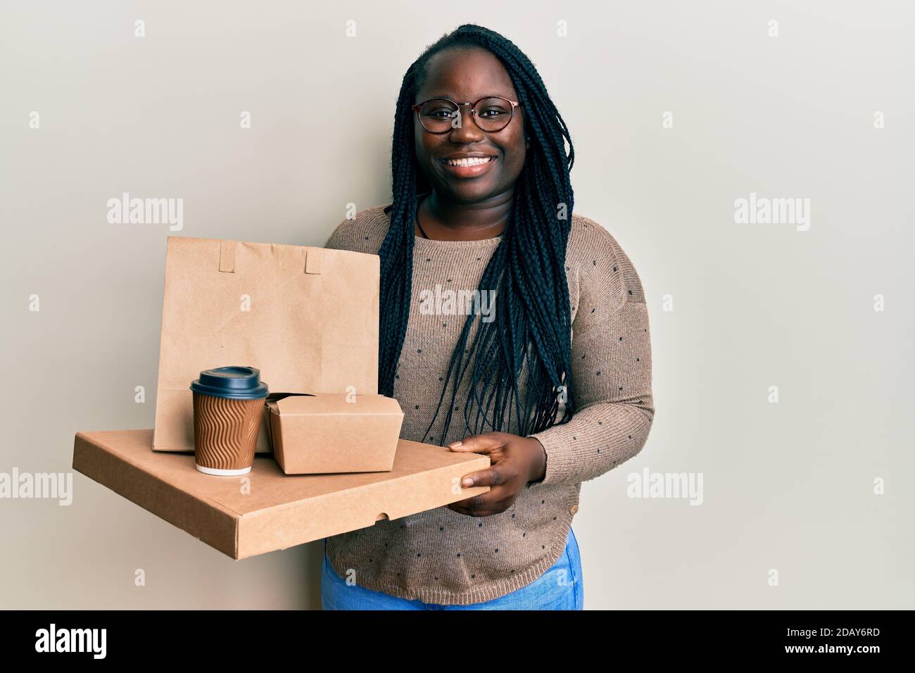 Young black woman with braids holding take away food smiling with a ...