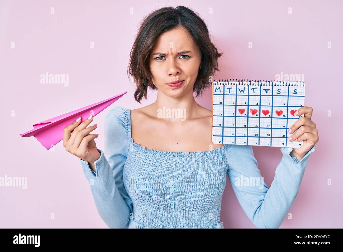 Young beautiful woman holding heart calendar and paper airplane skeptic ...