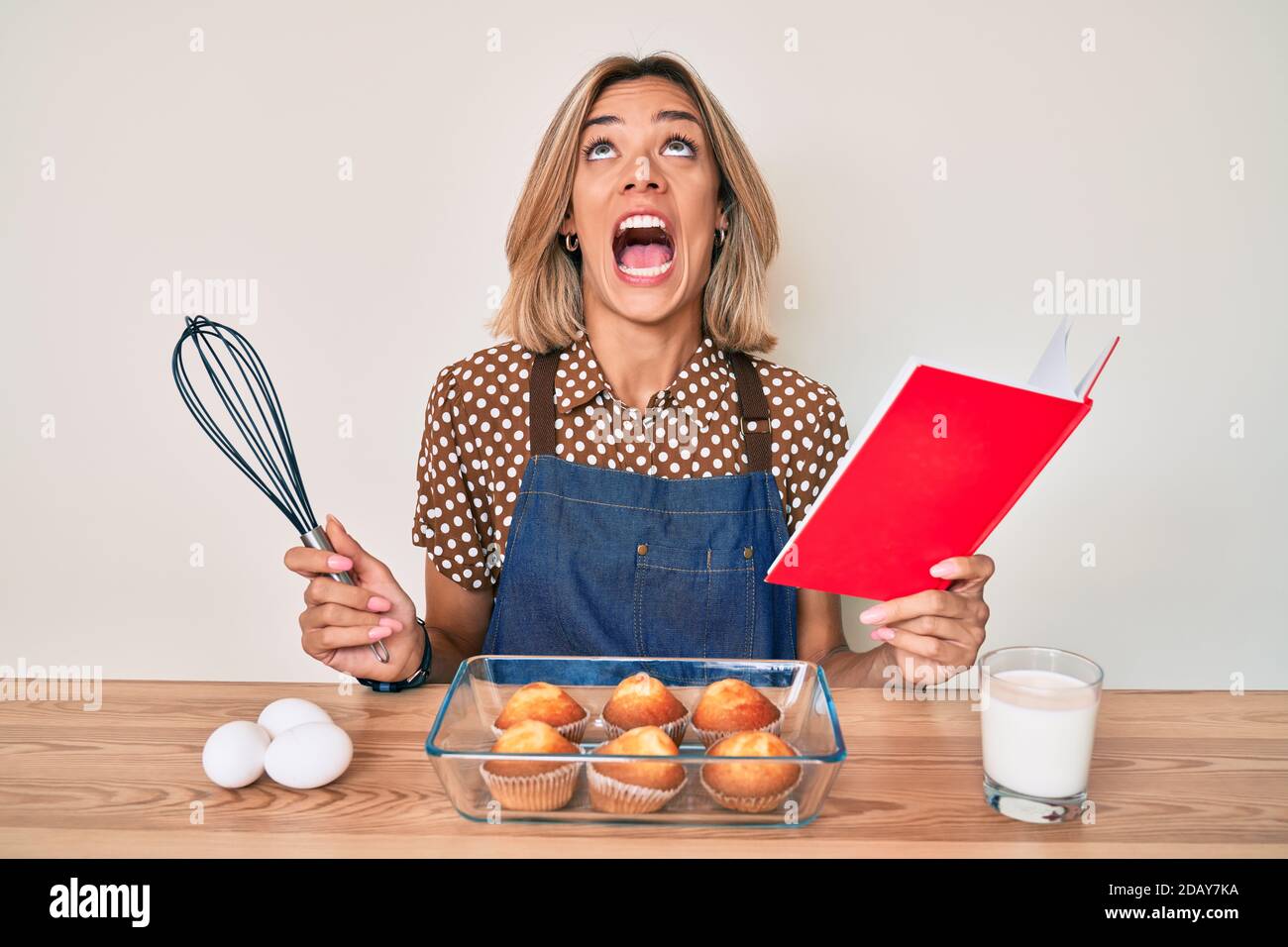 Beautiful caucasian woman wearing baker apron making muffins angry and ...