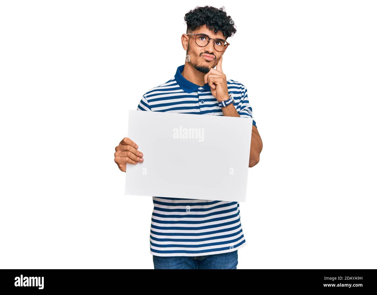 Young arab man holding blank empty banner serious face thinking about ...