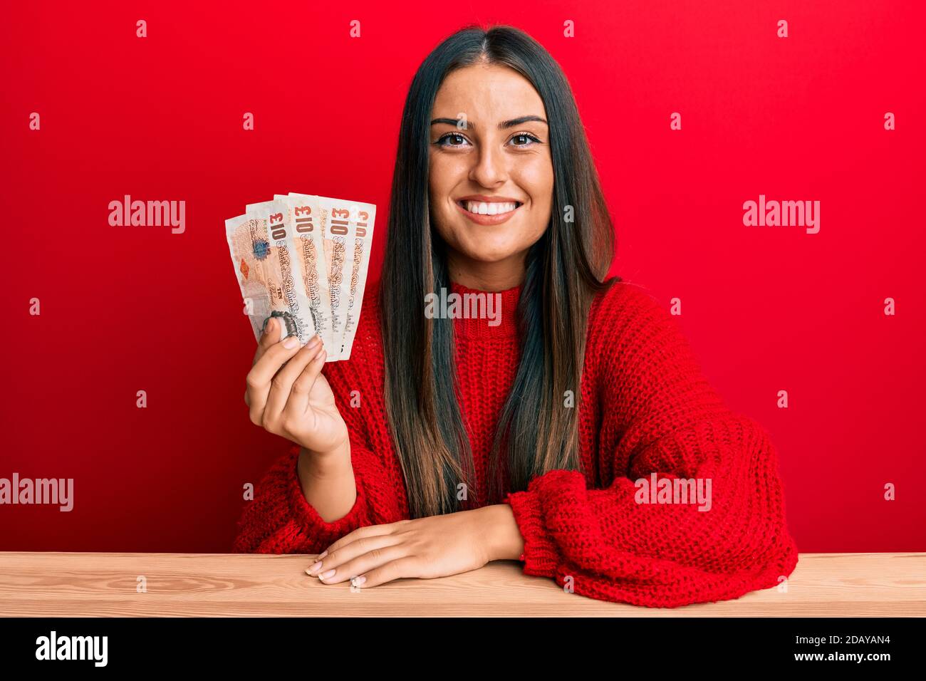 Beautiful hispanic woman holding united kingdom pounds looking positive ...