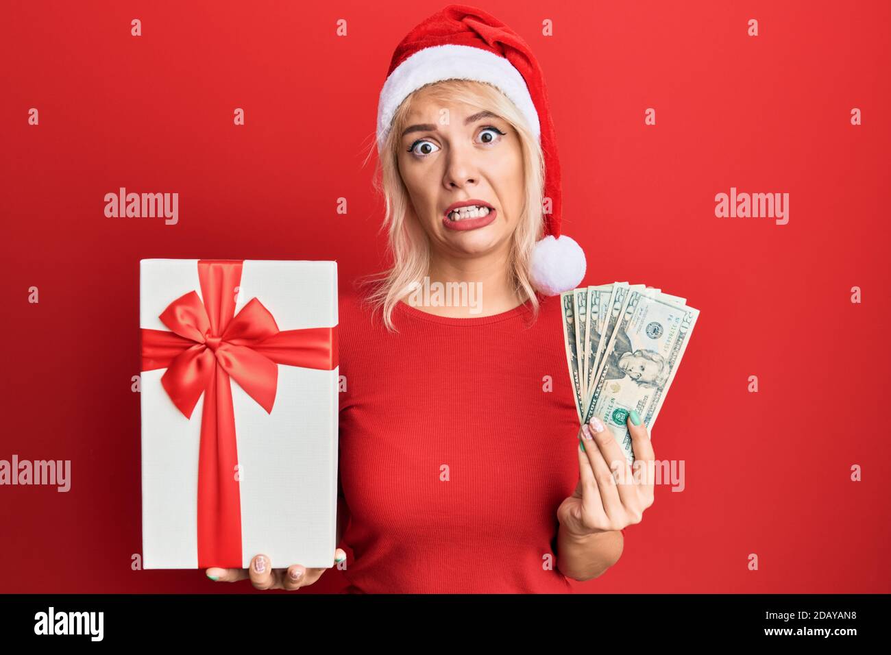 Young blonde girl wearing christmas hat, holding a gift and dollars ...