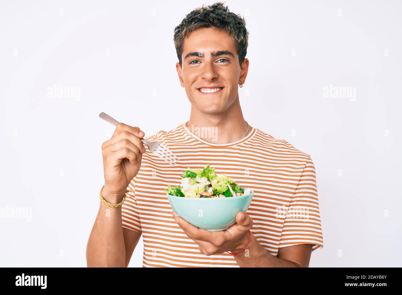Young handsome man eating salad smiling with a happy and cool smile on ...