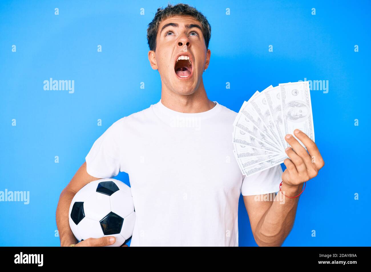 Young handsome man holding soccer ball and dollars banknotes angry and ...