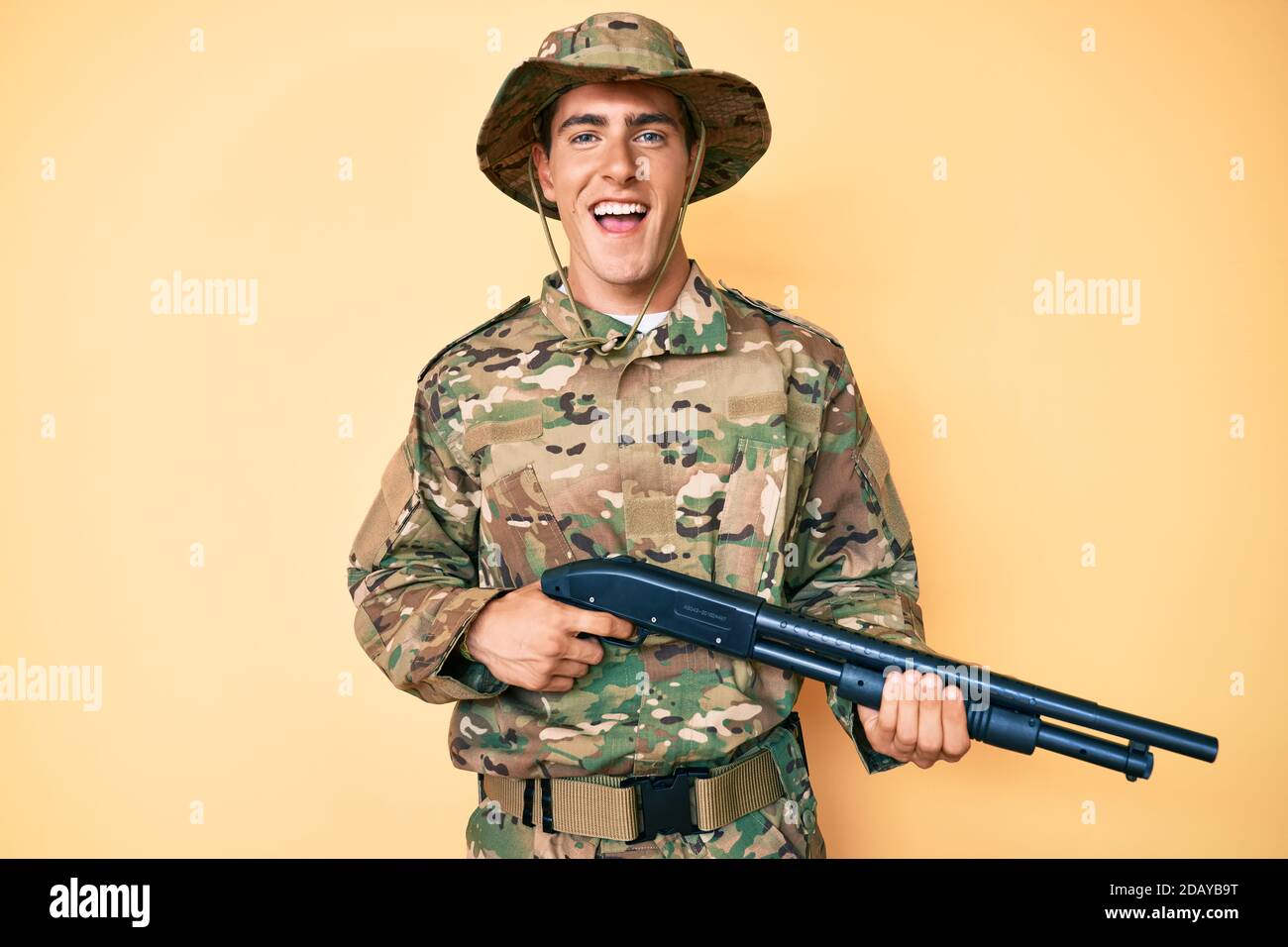 Young handsome man wearing camouflage army uniform holding shotgun ...