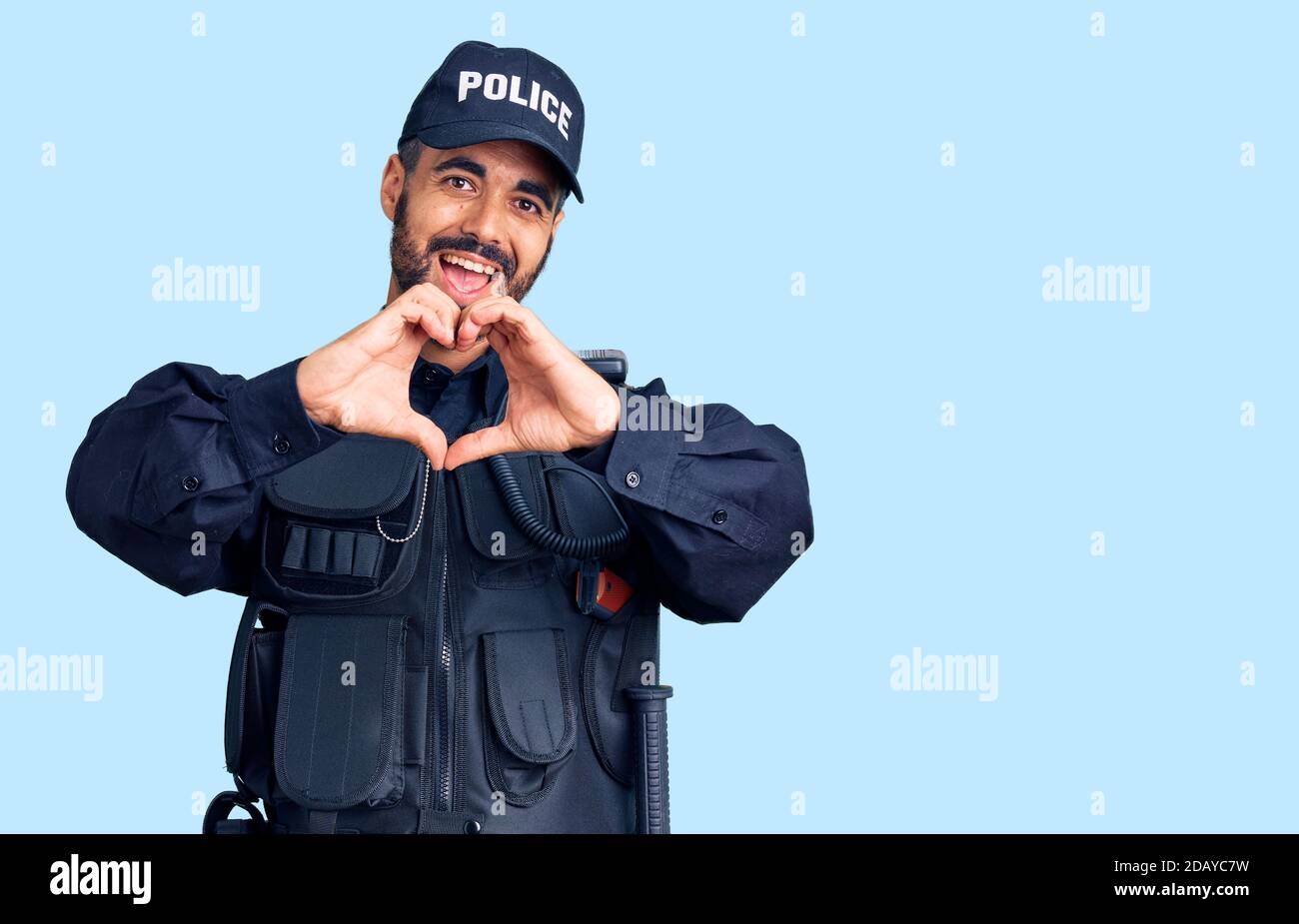 Young hispanic man wearing police uniform smiling in love doing heart ...