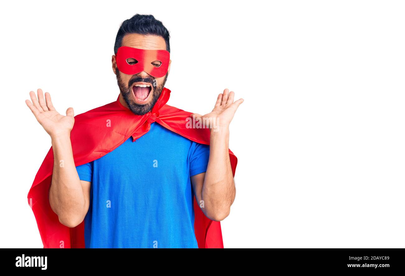 Young hispanic man wearing super hero costume celebrating mad and crazy ...