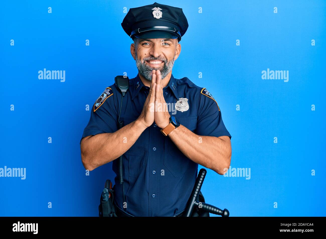 Middle age handsome man wearing police uniform praying with hands ...