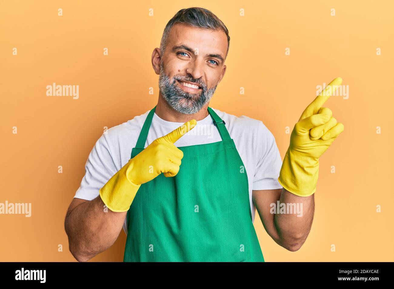 Middle age handsome man wearing cleaner apron and gloves smiling and ...