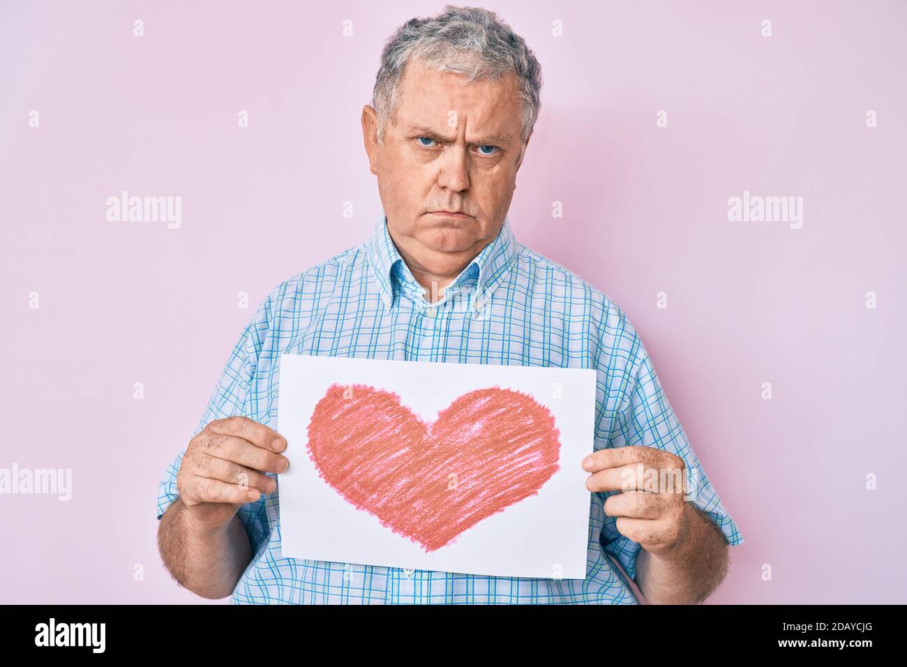 Senior grey-haired man holding heart draw skeptic and nervous, frowning ...