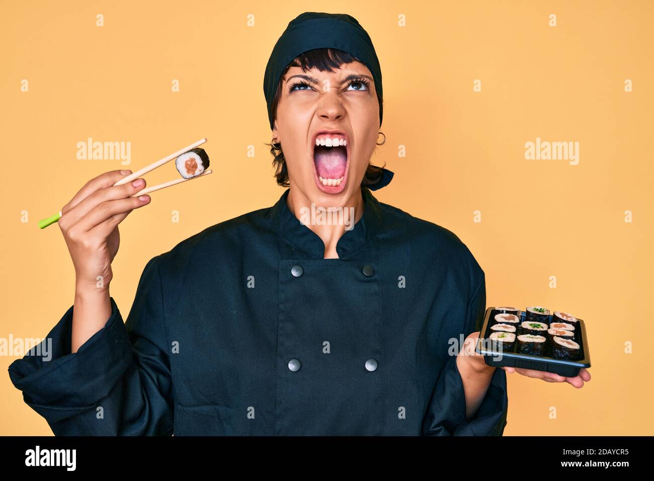 Beautiful brunettte woman chef holding sushi using chopsticks angry and ...