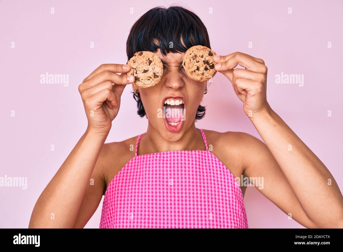 Beautiful brunettte woman holding chocolate chips cookies on eyes angry ...