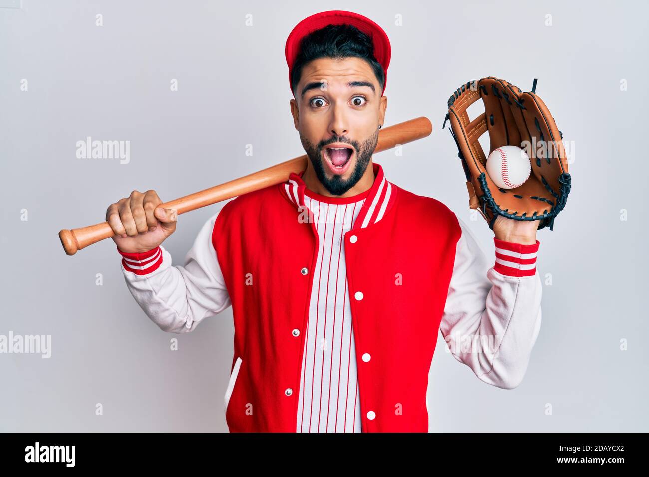 Young man with beard playing baseball holding bat and ball afraid and ...