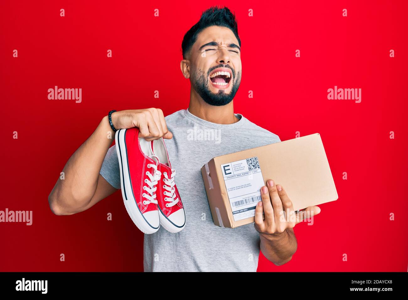 Young man with beard taking casual red shoes from box angry and mad ...