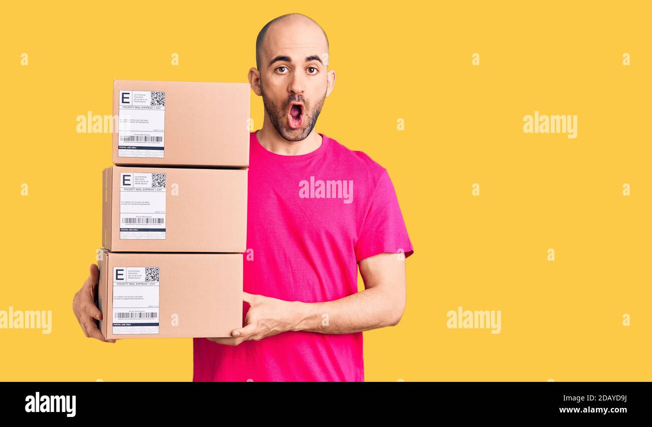 Young handsome man holding delivery package scared and amazed with open ...