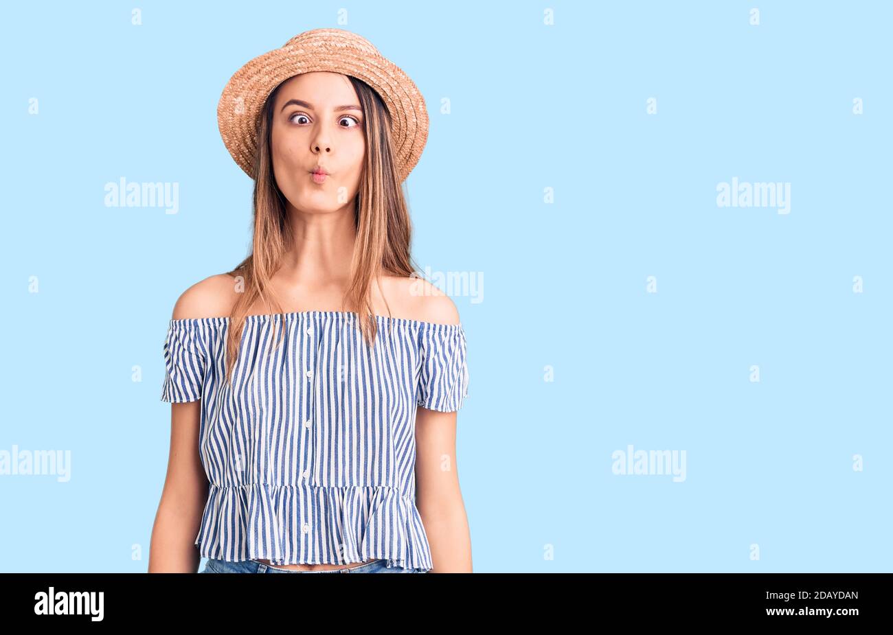 Young beautiful girl wearing hat and t shirt making fish face with lips ...