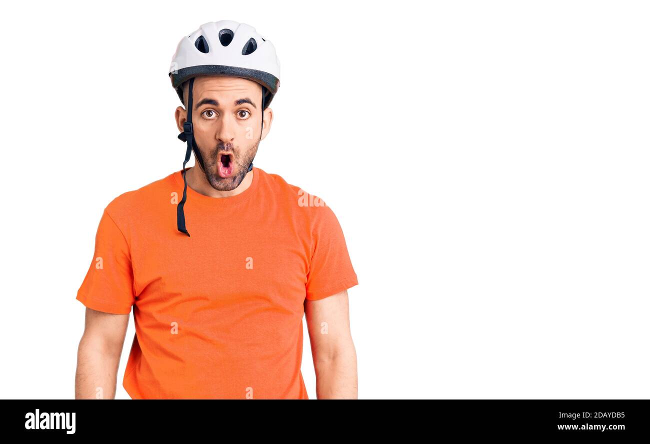 Young handsome man wearing bike helmet scared and amazed with open ...