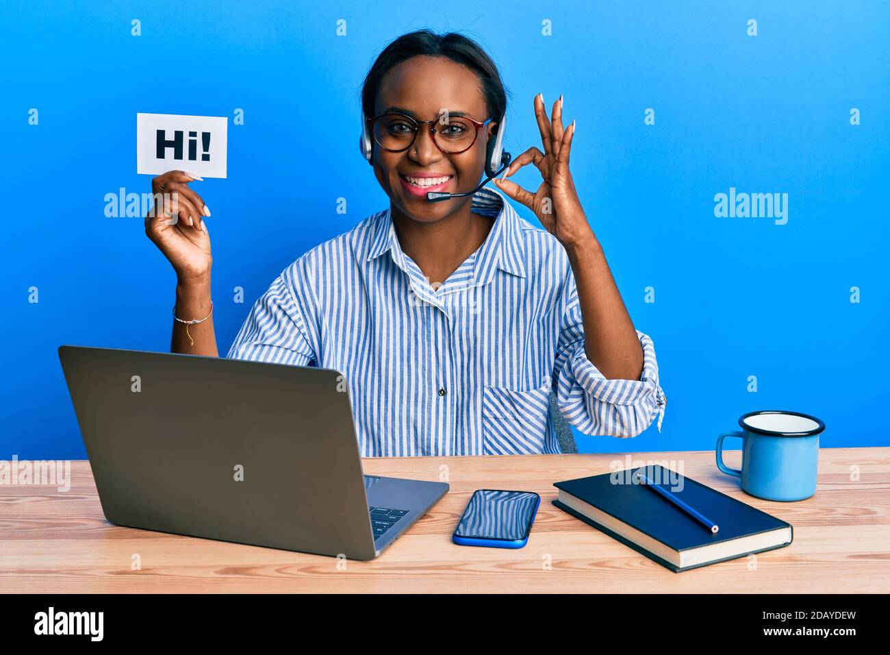 Young african woman wearing operator headset holding hi word doing ok ...