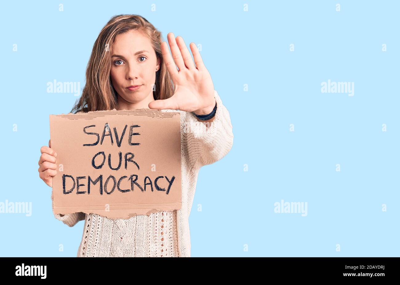 Young beautiful blonde woman holding save our democracy banner with ...