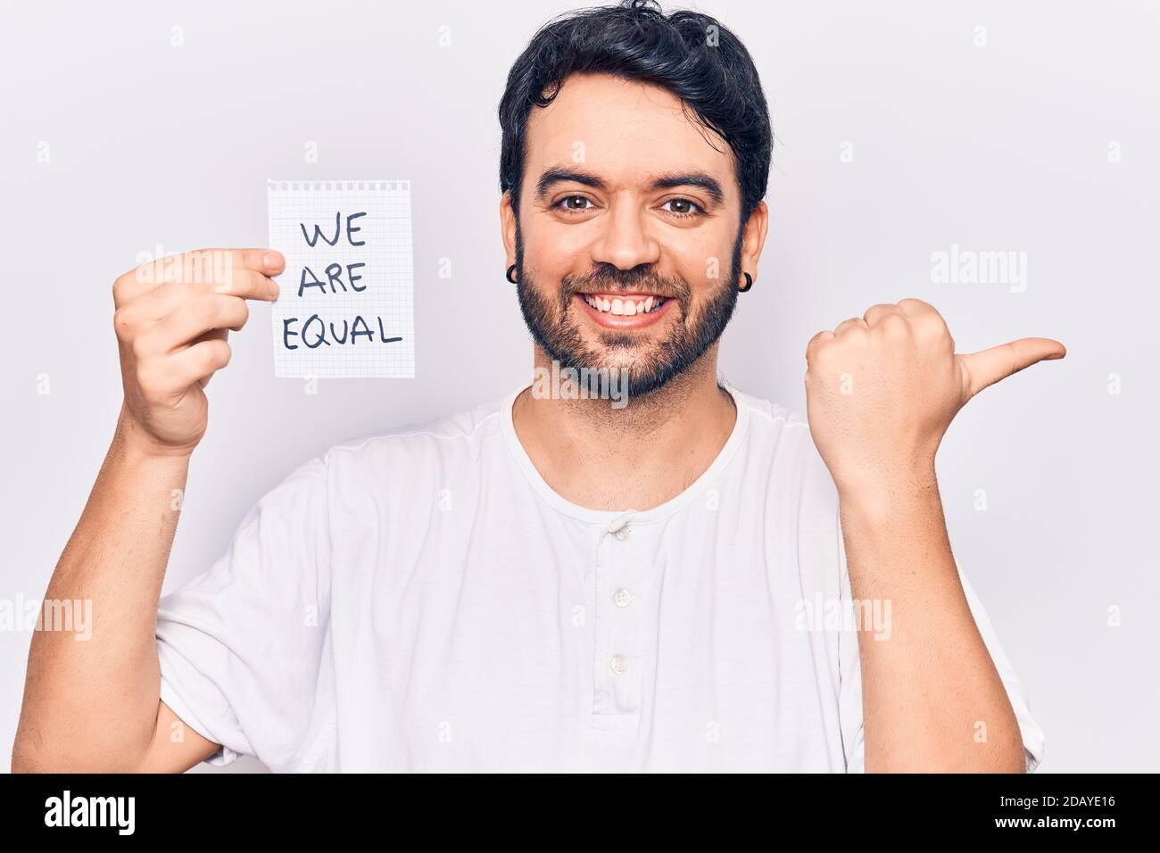 Young hispanic man holding we are equal paper pointing thumb up to the ...