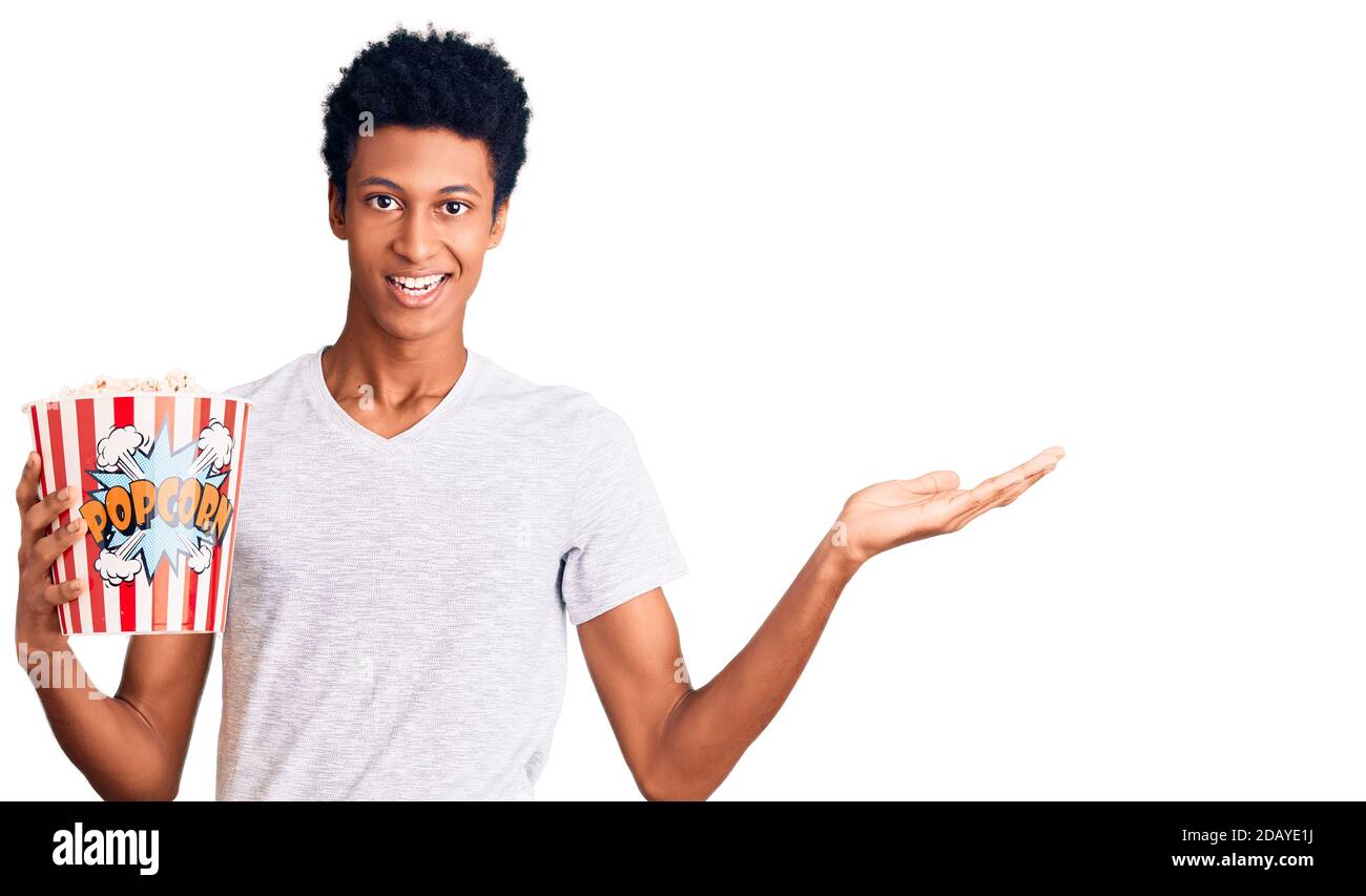 Young african american man holding popcorn celebrating victory with happy smile and winner ...