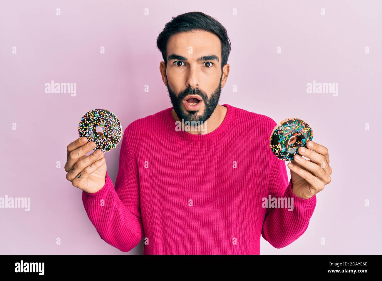 Young hispanic man with beard holding tasty colorful doughnuts relaxed ...