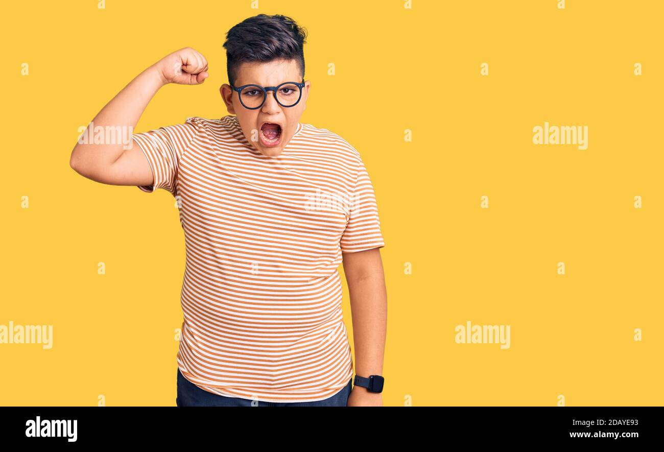 Little boy kid wearing casual clothes and glasses angry and mad raising ...