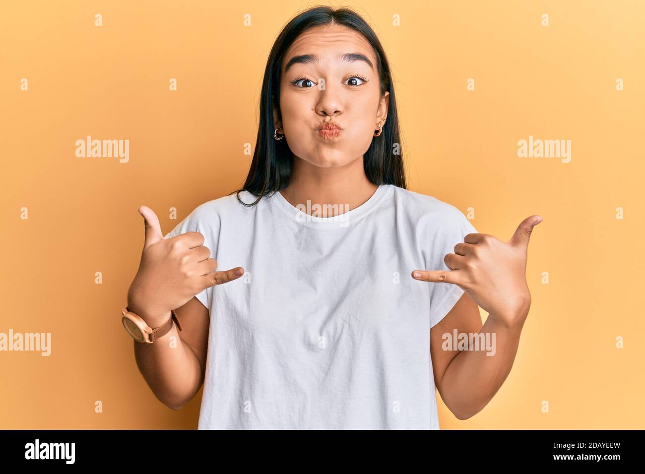 Young asian woman doing shaka sign with hands puffing cheeks with funny ...