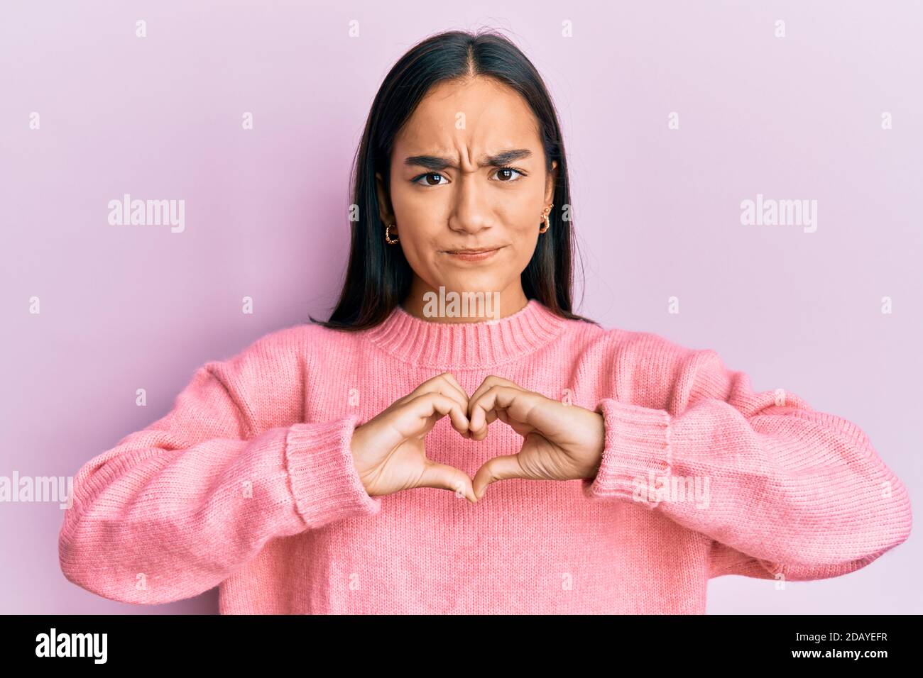 Young asian woman doing heart symbol with hands skeptic and nervous ...