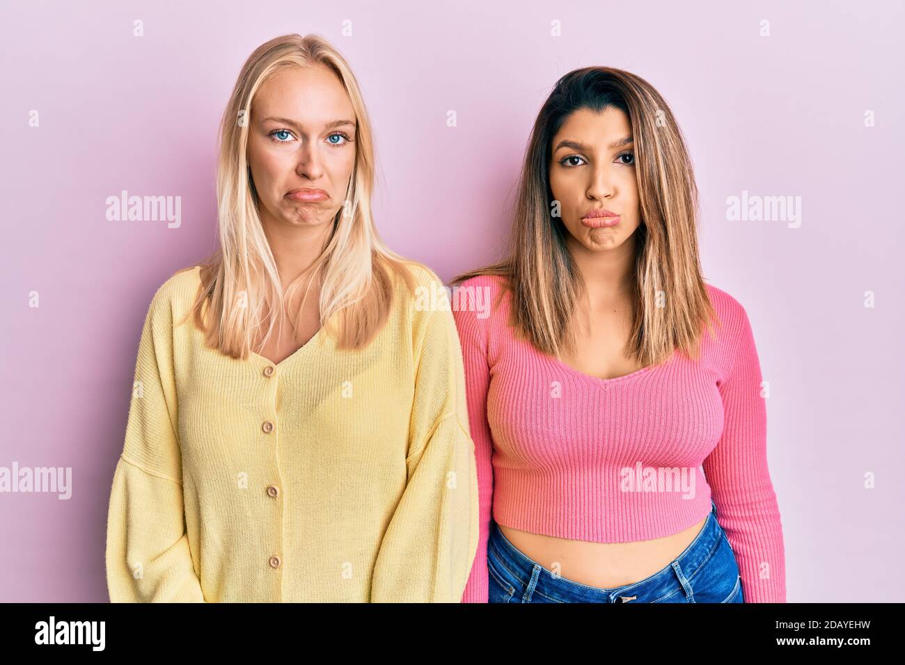 Two friends standing together over pink background depressed and worry ...