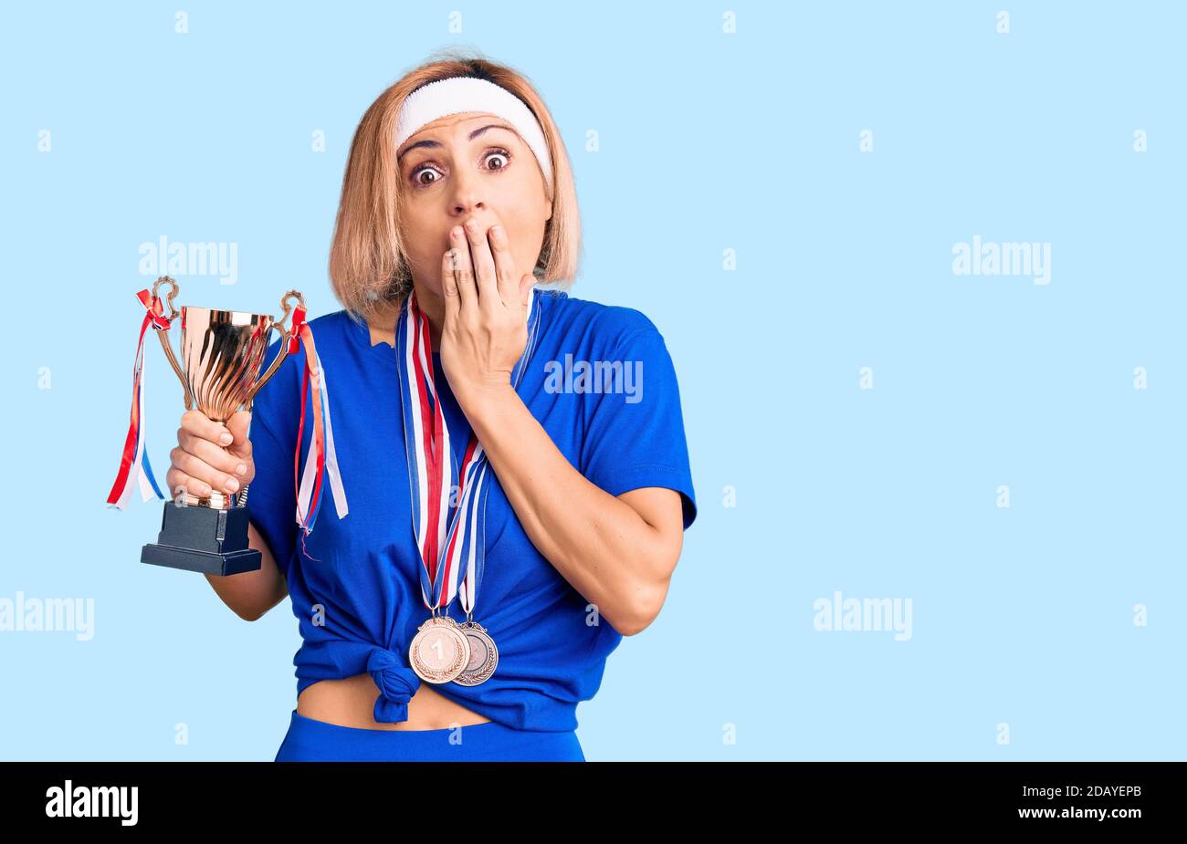 Young blonde woman holding champion trophy wearing medals covering ...