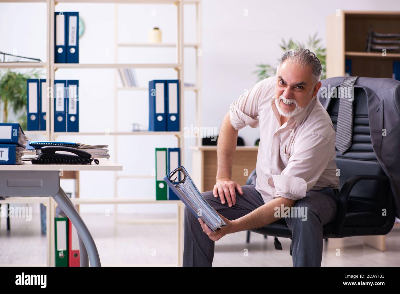 Senior male employee doing physical exercises at workplace Stock Photo ...