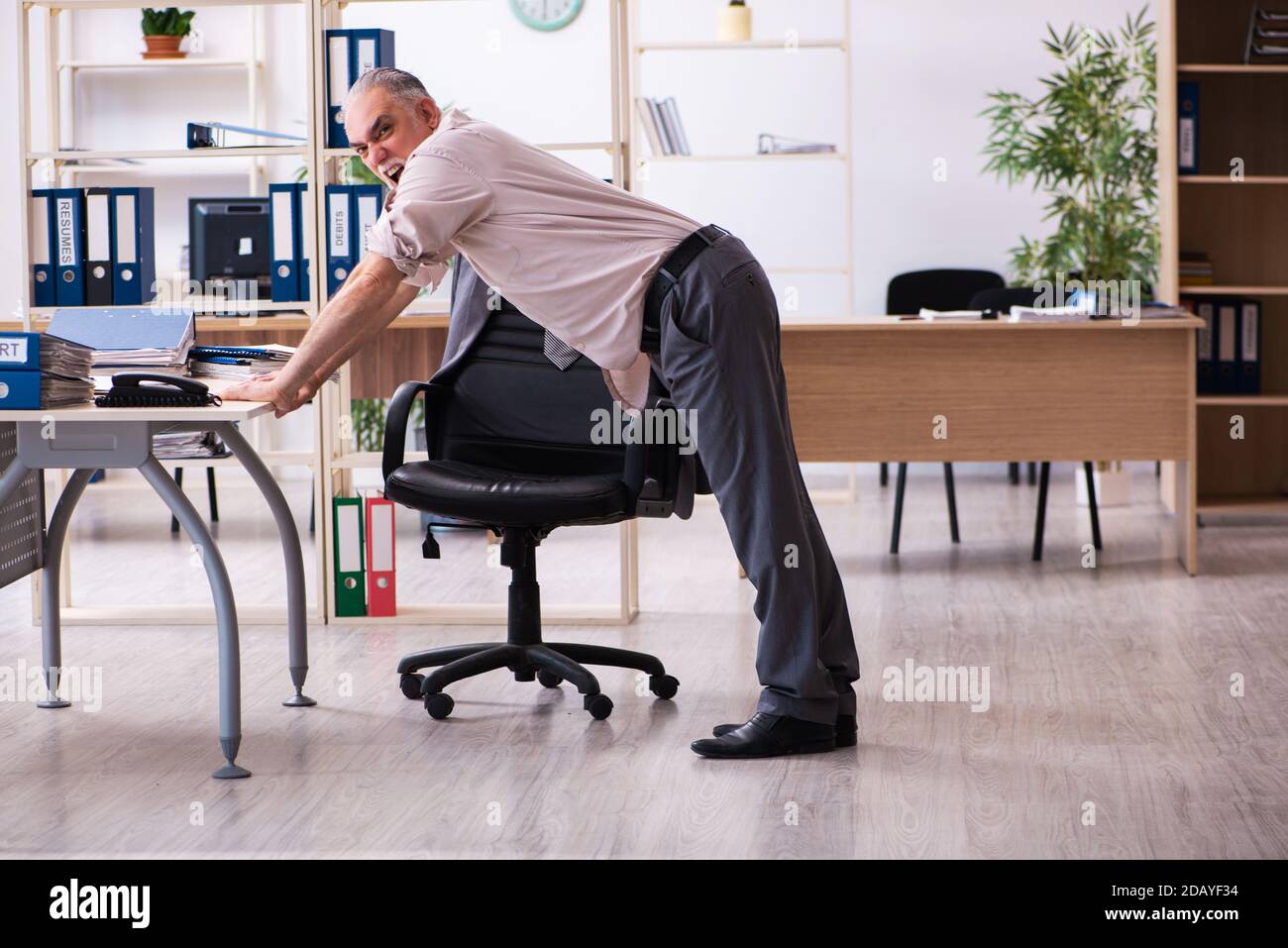 Senior male employee doing physical exercises at workplace Stock Photo ...