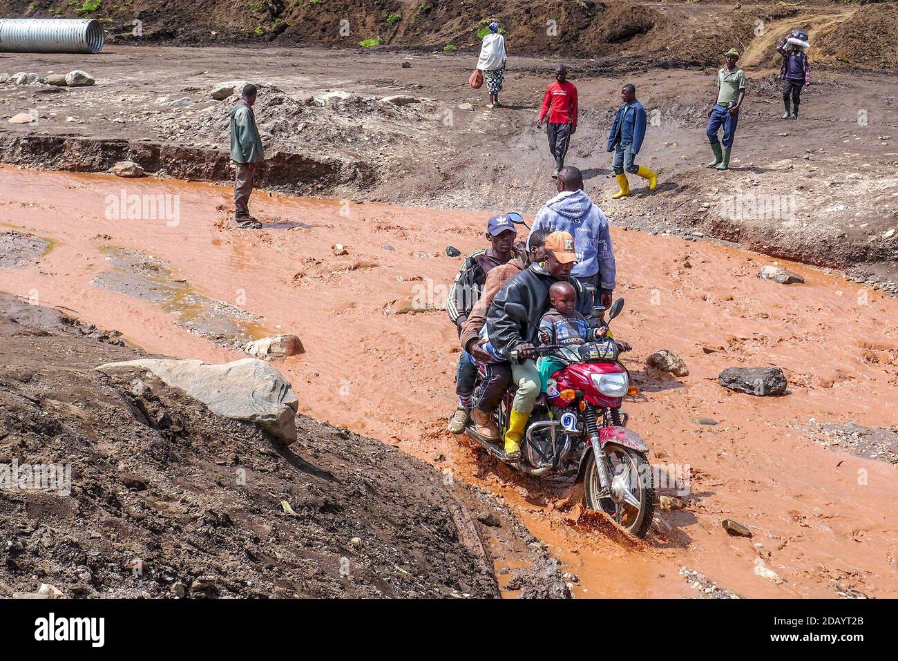People ride a motorcycle on a muddy, unpaved road that stretches ...