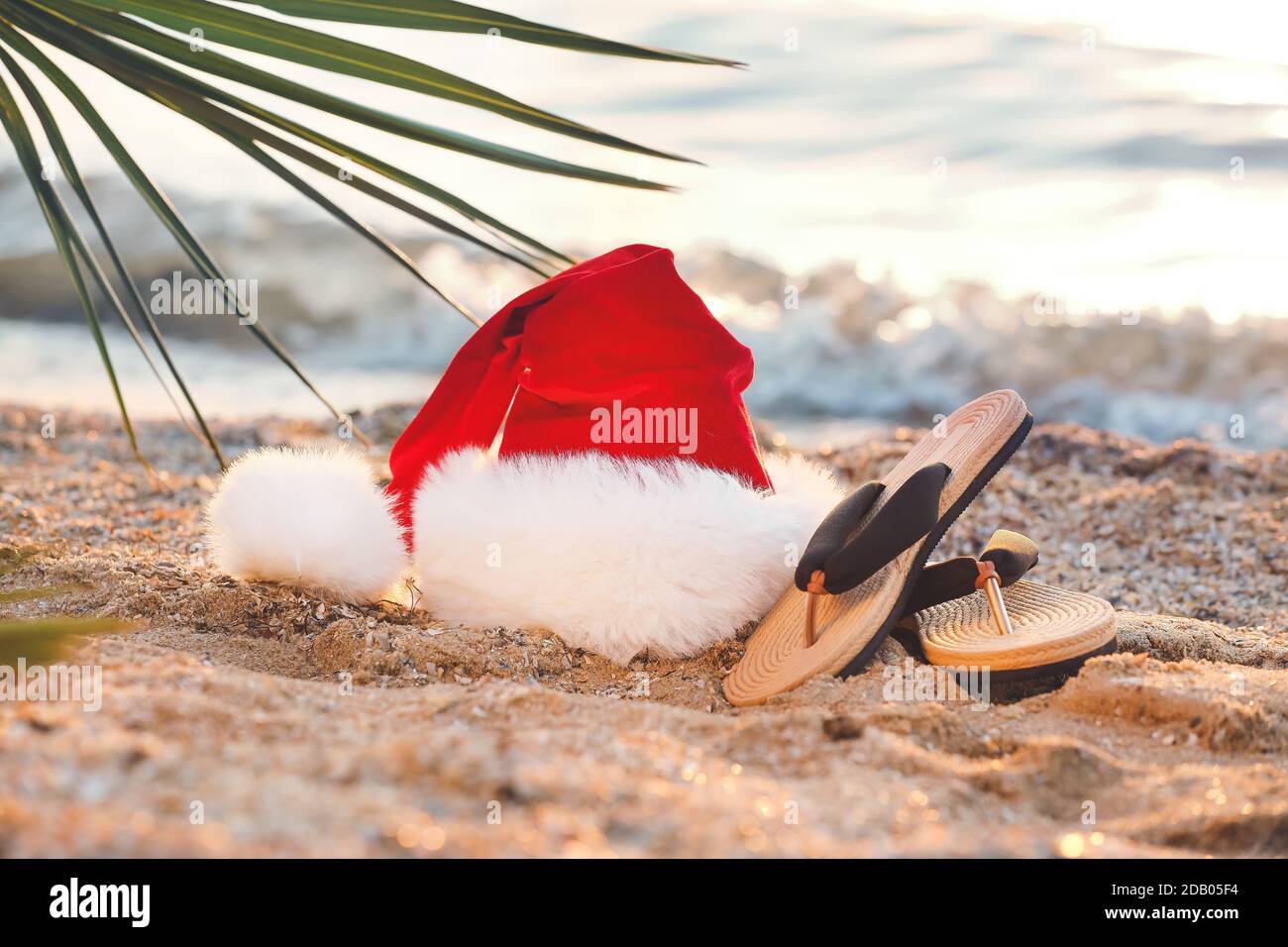 Santa hat, tropical leaf and flip-flops on sea beach. Christmas ...