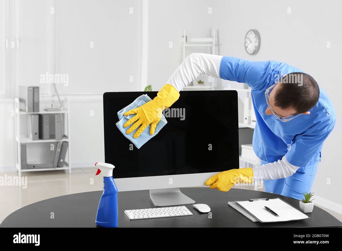 Male janitor cleaning computer in office Stock Photo - Alamy