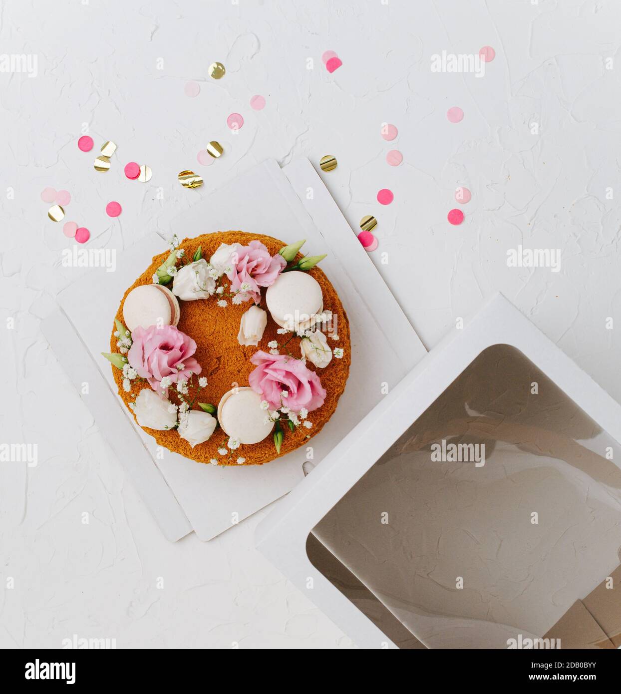 Top view of a honey cake with flowers on a box base next to windowed ...