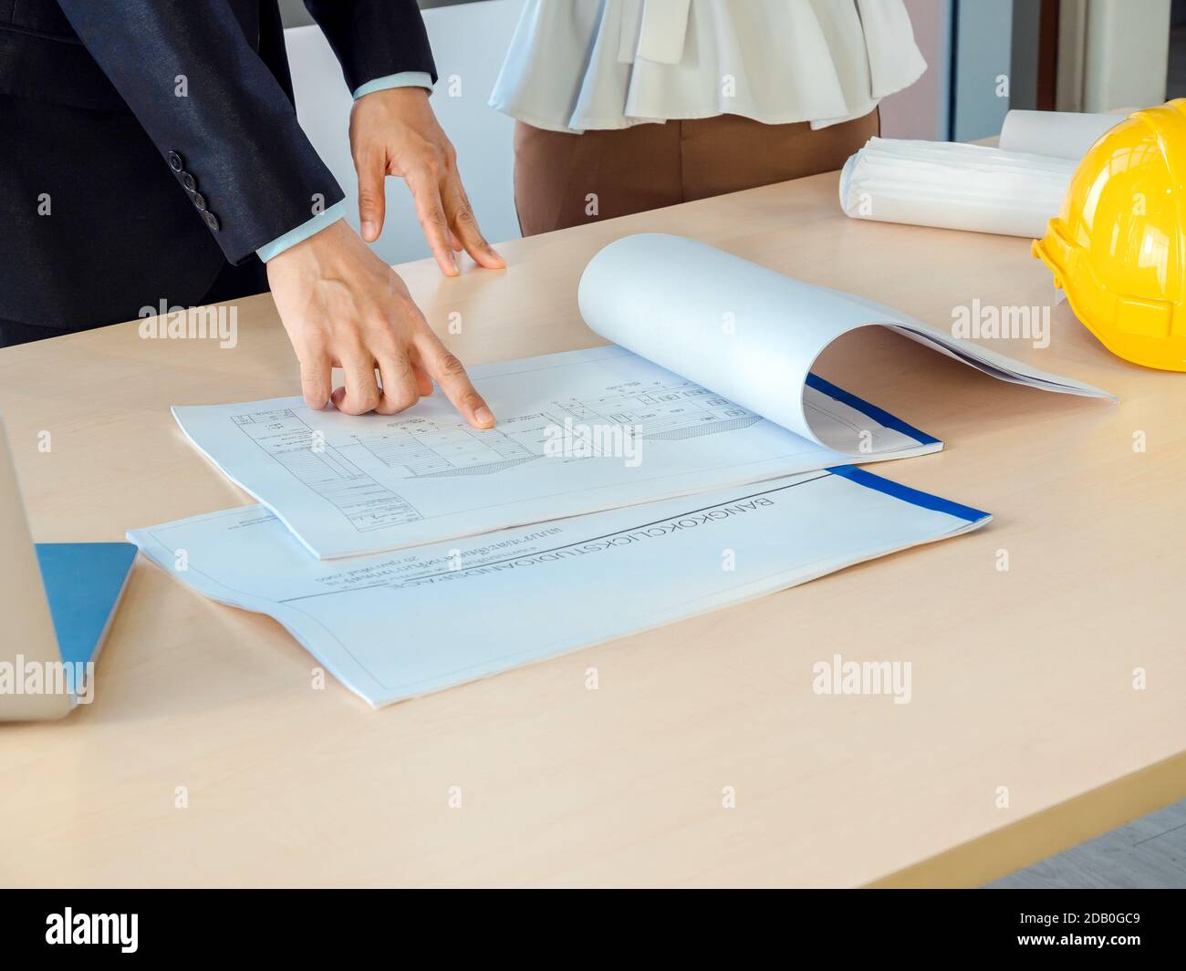 Engineer hand pointing blueprint on wooden desk with safety hard hat ...